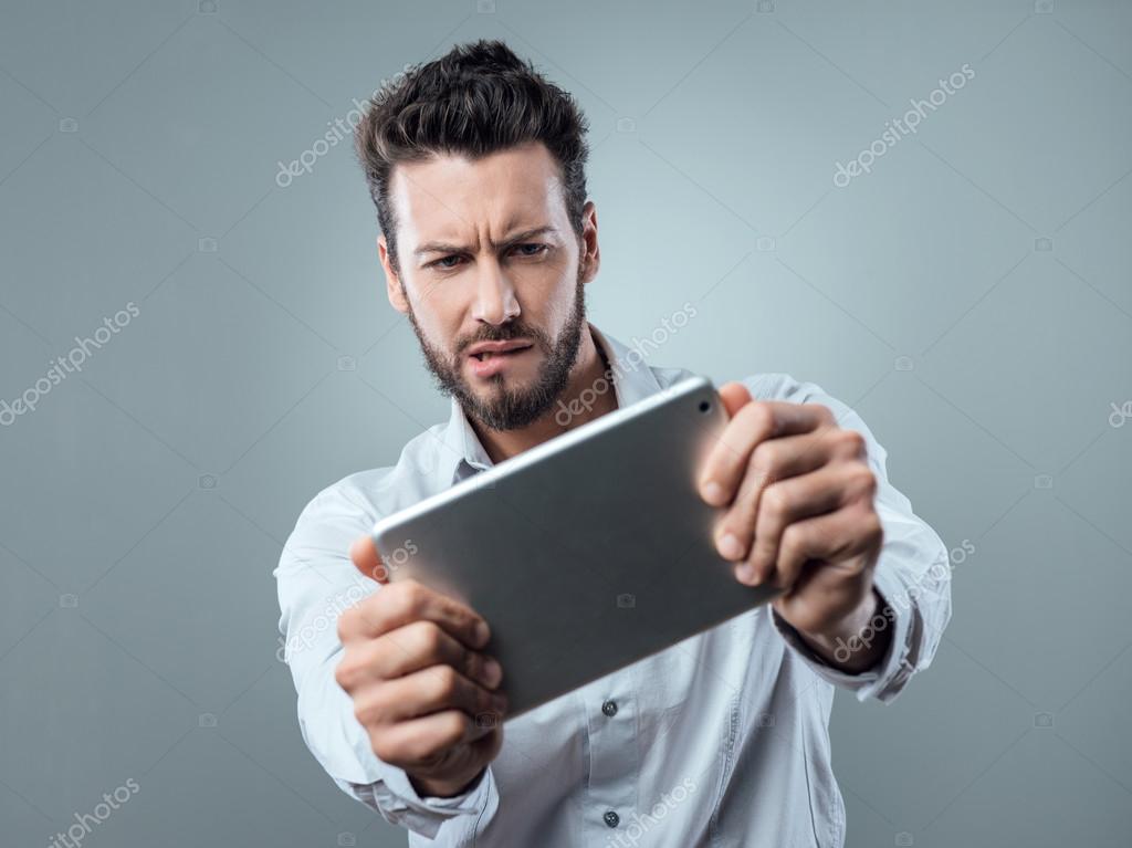 Confused man watching his tablet Stock Photo by ©stokkete 82872954