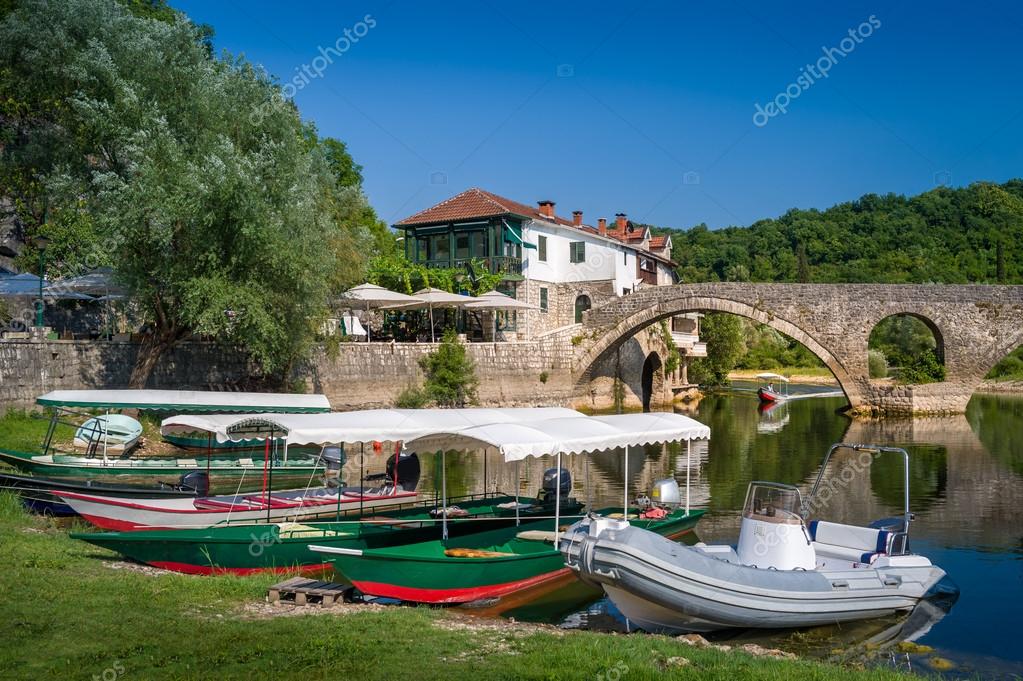 Rijeka Crnojevica old town excursion boats moored. Ancient arch bridge at background. Stock ...