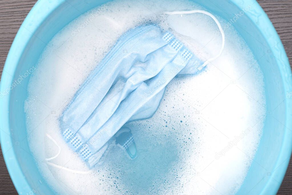 Máscara médica desechable remojo en lavabo de plástico azul con agua ...