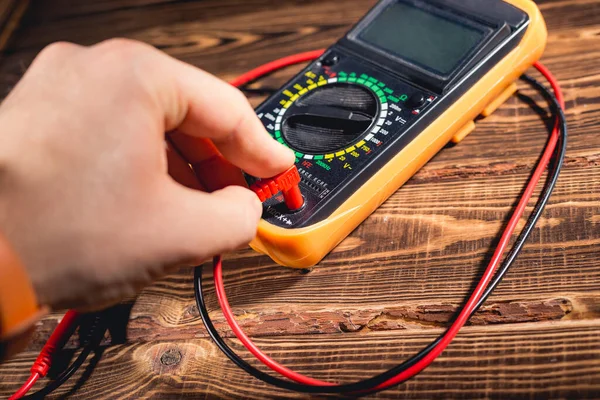 Multimeter and two test leads on a wooden background. A man's hand ...
