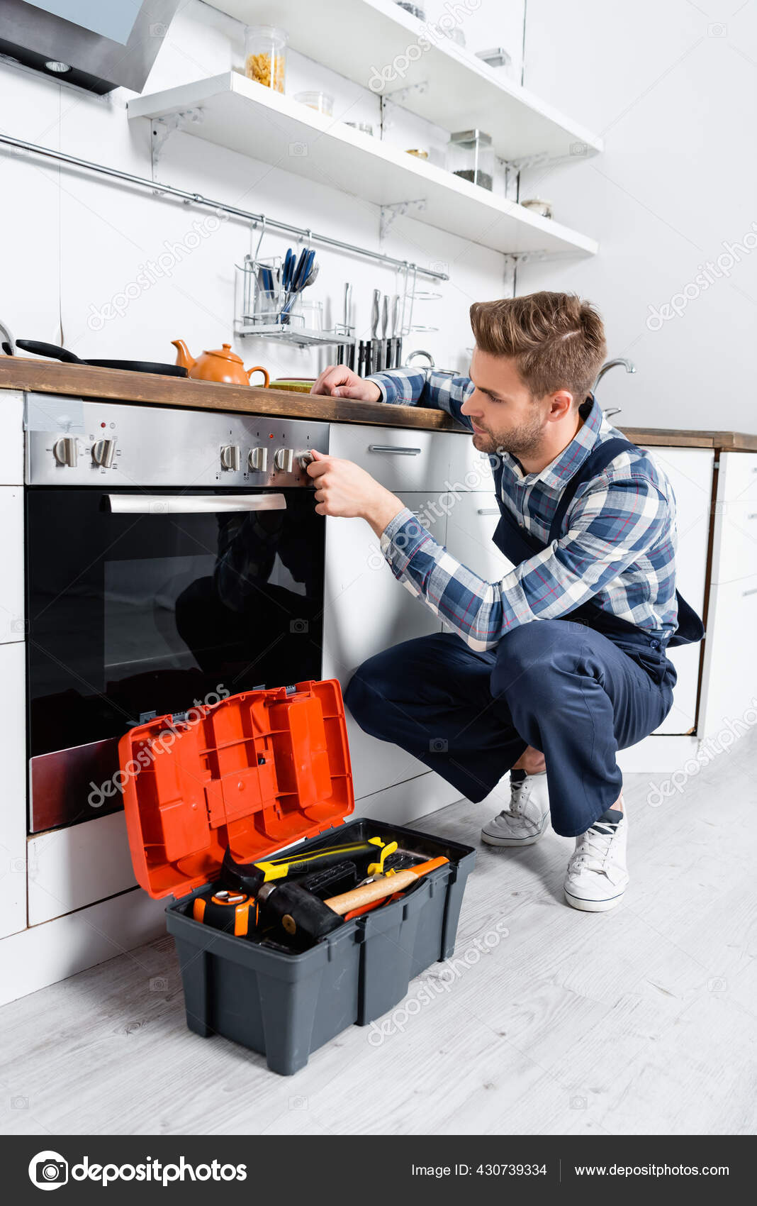 Full Length Young Handyman Checking Oven Button While Sitting Toolbox ...