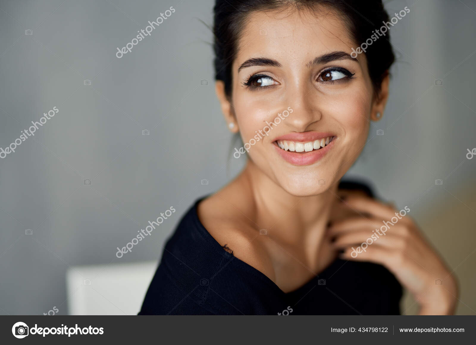Beautiful Lydia With evening make-up in a black dress sits indoors on a ...
