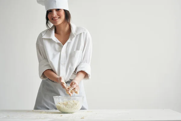 cheerful woman baker in chefs uniform rolls the dough on the table work ...
