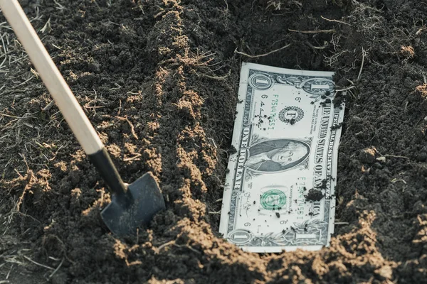 a shovel near the dug hole in it a dollar, bury the money in the ground ...