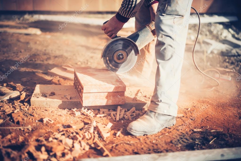 Worker using an angle grinder on construction site for cutting bricks ...