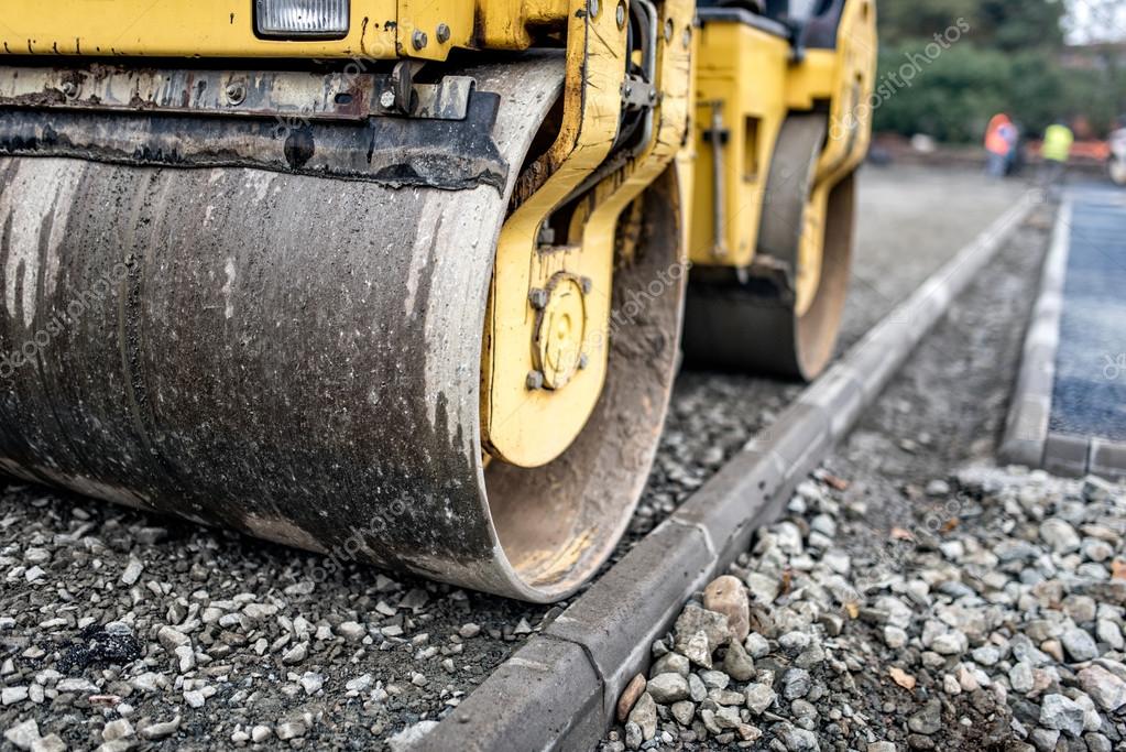Heavy tandem road roller compacting layers of gravel on road ...