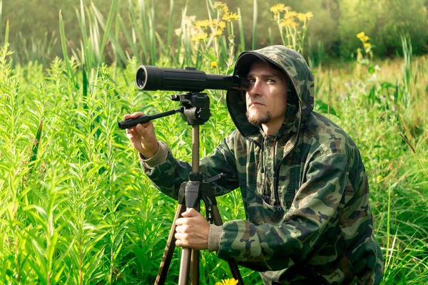 man birdwatcher with a spotting scope and notepad among the tall grass ...