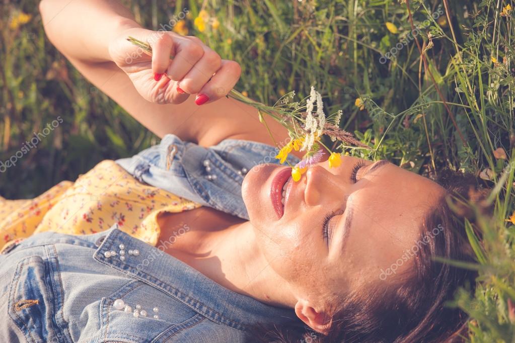 Beautiful girl smiling and lying on field and holding flowers in ...