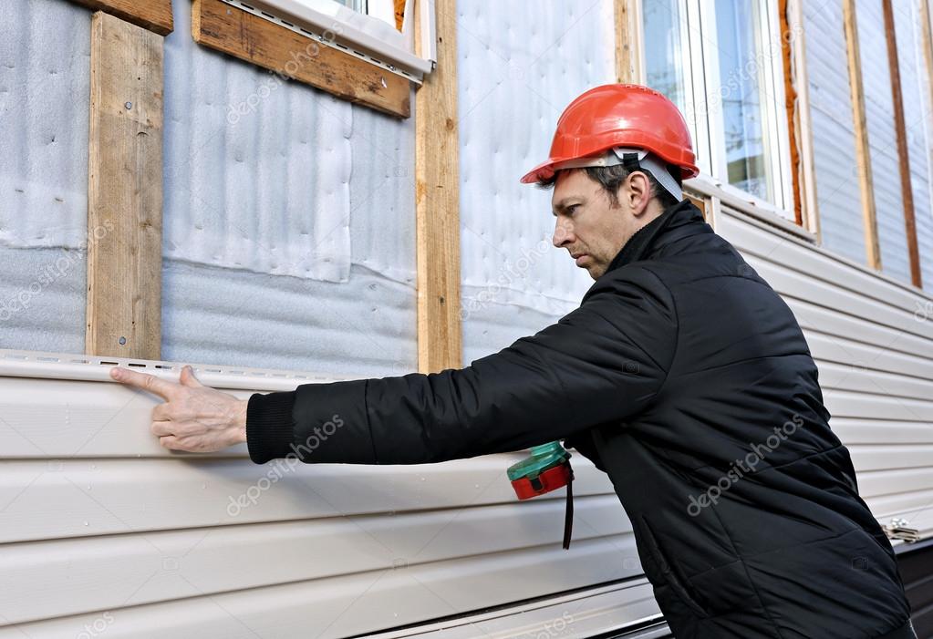 A worker installs panels beige siding on the facade of the house ...