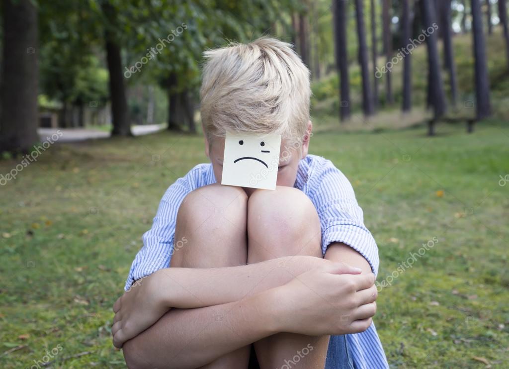 Crying boy sits on green grass in forest. Concept of sad thought ...