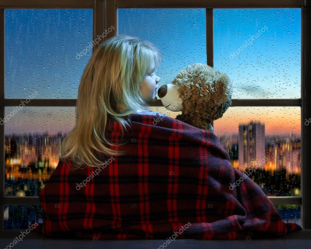 Little girl talking with a toy bear in the window. Outside, the late ...