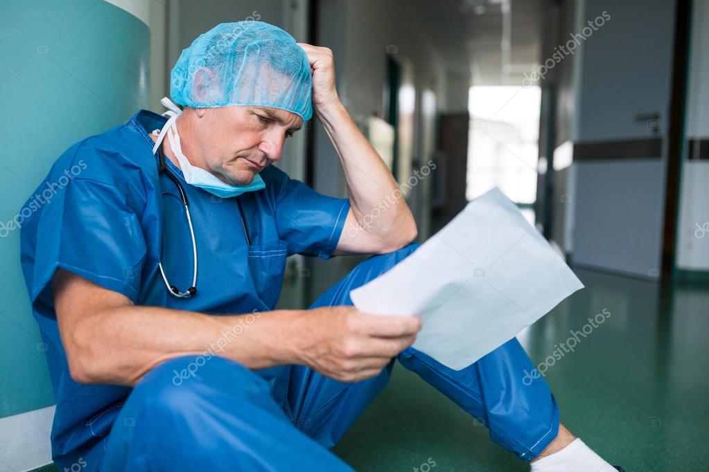 Sad surgeon sitting on floor with report Stock Photo by ©Wavebreakmedia ...