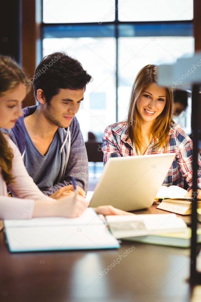 Estudiante mirando a la cámara mientras estudia con compañeros de clase ...