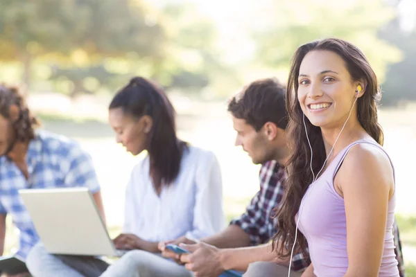 Smiling friends using media devices in park - Stock Image - Everypixel