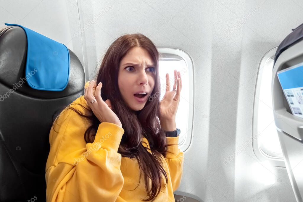 Una chica se sienta frente a una ventana de avión y está nerviosa ...
