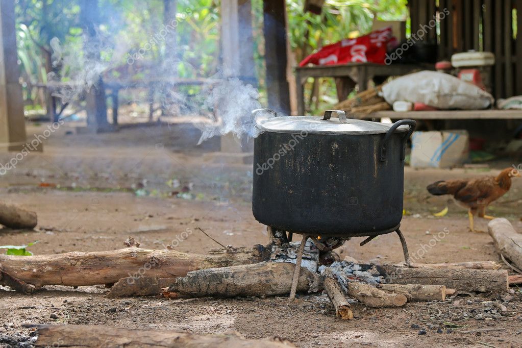Hot steam coming out through lid on black boiling pot above wood ...