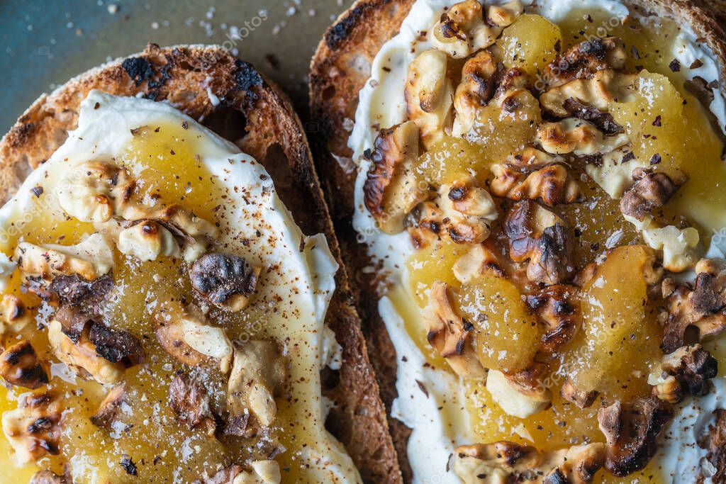Dos tostadas de pan con queso crema, nueces asadas, miel, pimienta y sal en el plato, de cerca ...
