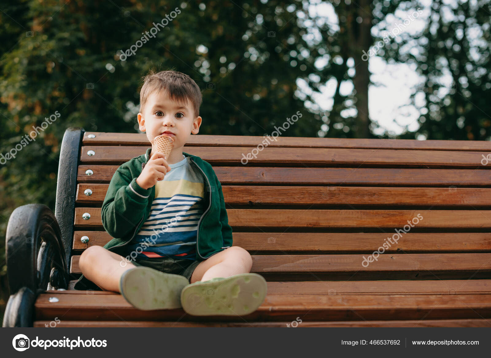 Small boy is eating an ice cream while sitting on the bench in the park ...