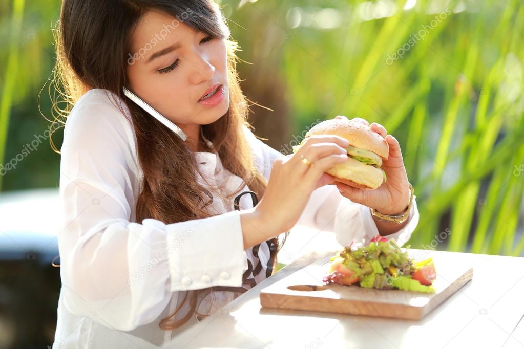 Multitasking woman talking on the phone while eating burger Stock Photo ...