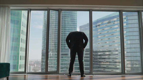 A businessman stands at the window against the backdrop of skyscrapers ...