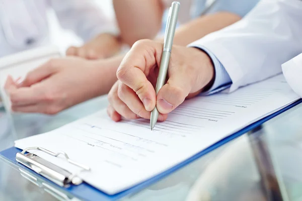 Doctors hands holding pen over paper ready to prescribe pills to ...