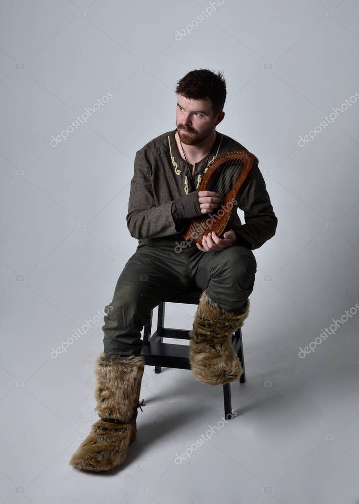 Retrato de cuerpo entero del joven guapo vestido con traje medieval de aventurero celta tocando ...