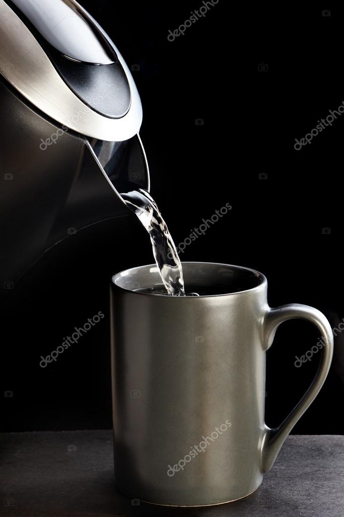 Tetera moderna vertiendo agua en la taza aislada en negro 2023