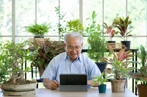 A retired old man use wireless communication via a tablet computer to ...