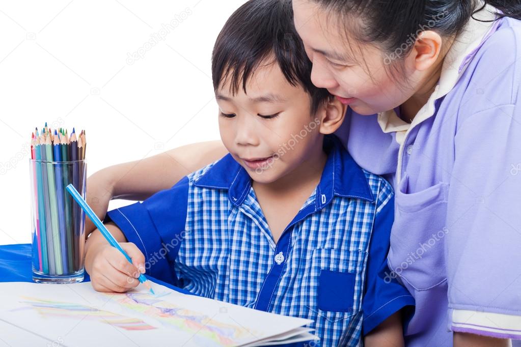 Little asian boy sitting at the table and drawing by colour penc ...