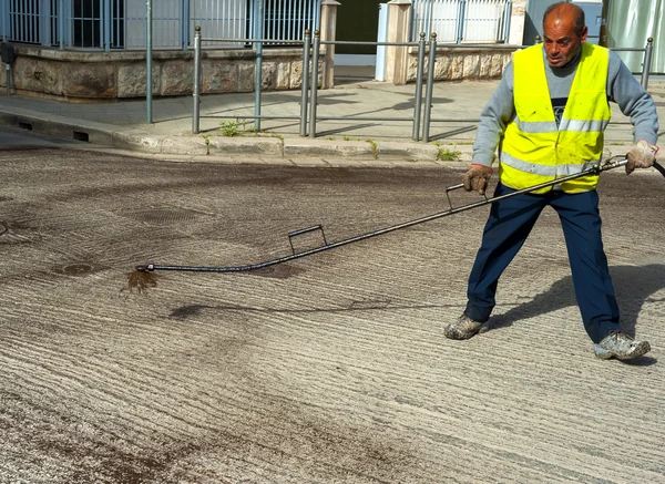 Road worker spraying bitumen emulsion with the hand spray lance before ...