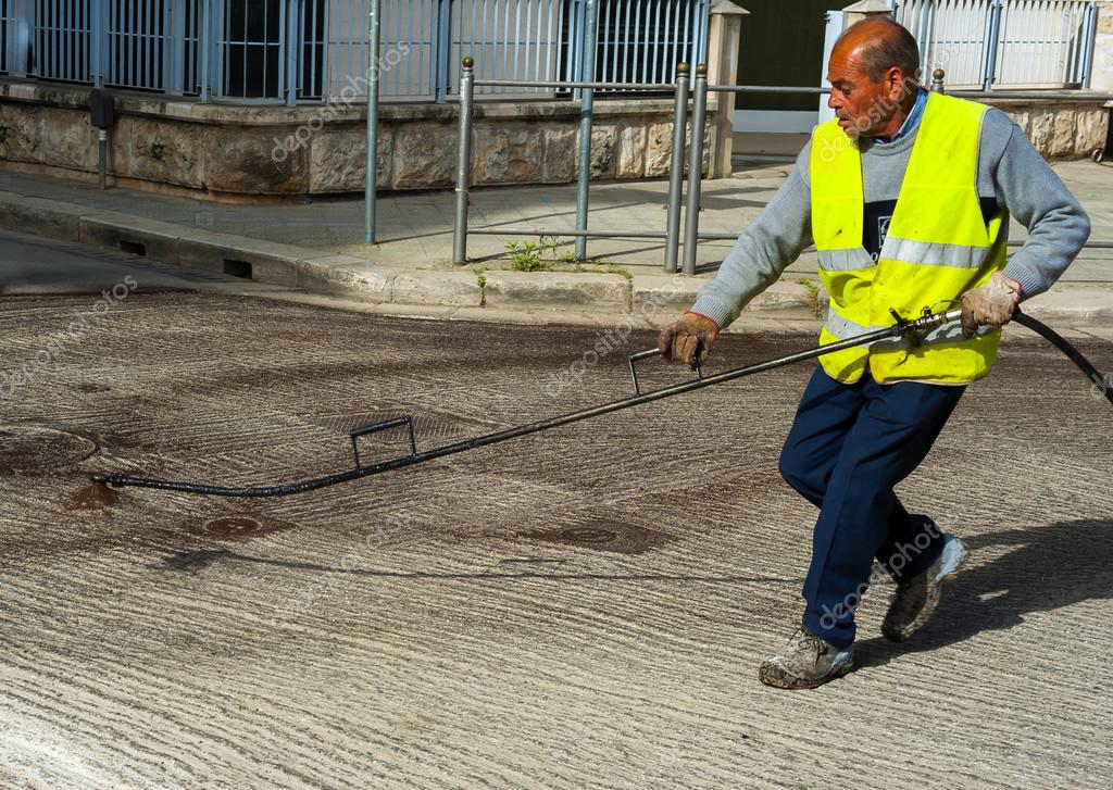 Road worker spraying bitumen emulsion with the hand spray lance before ...