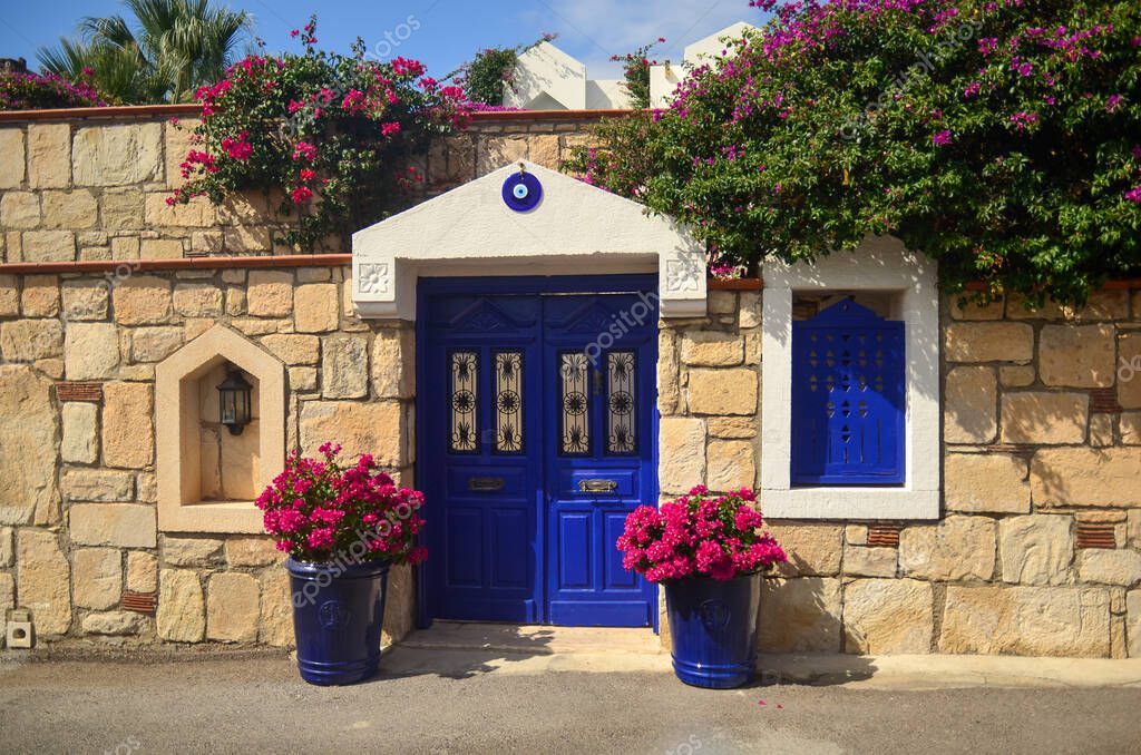 Edificio antiguo de piedra (casa) con puerta y ventanas vintage de madera azul. Hermosas flores ...