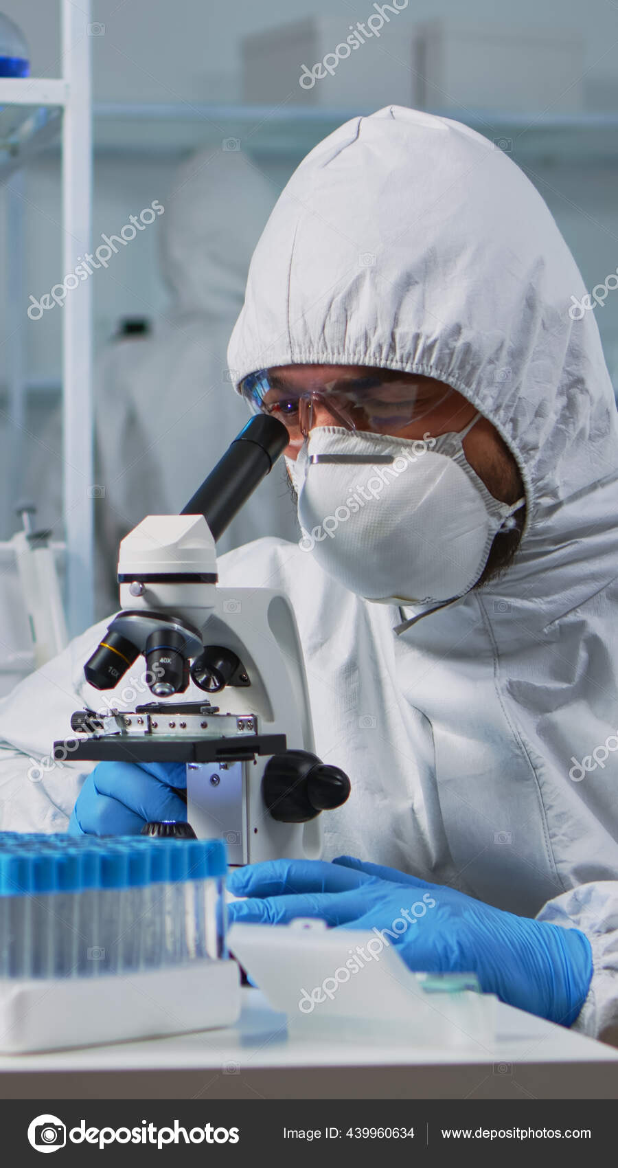 Close up of scientist looking through a microscope wearing ppe suit ...