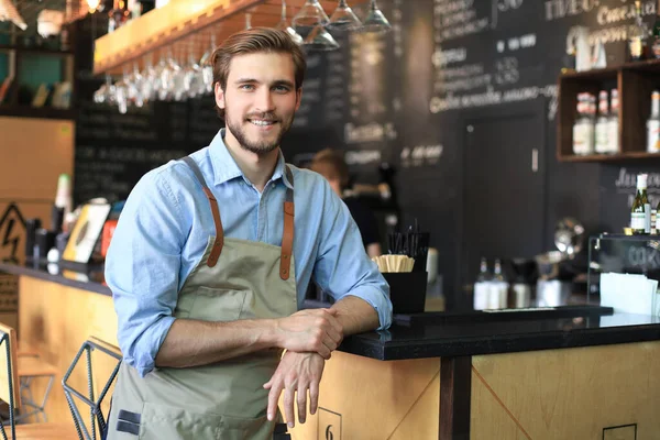 Shot of happy young bar owner standing near the counter and looking at ...