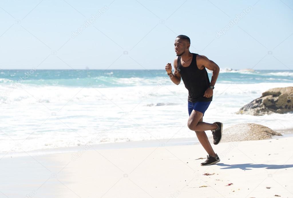 Active african american man running by water on the beach Stock Photo ...