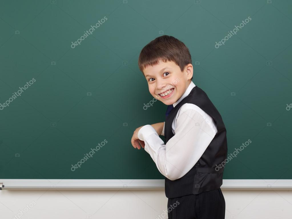 School student boy posing at the clean blackboard, grimacing and ...