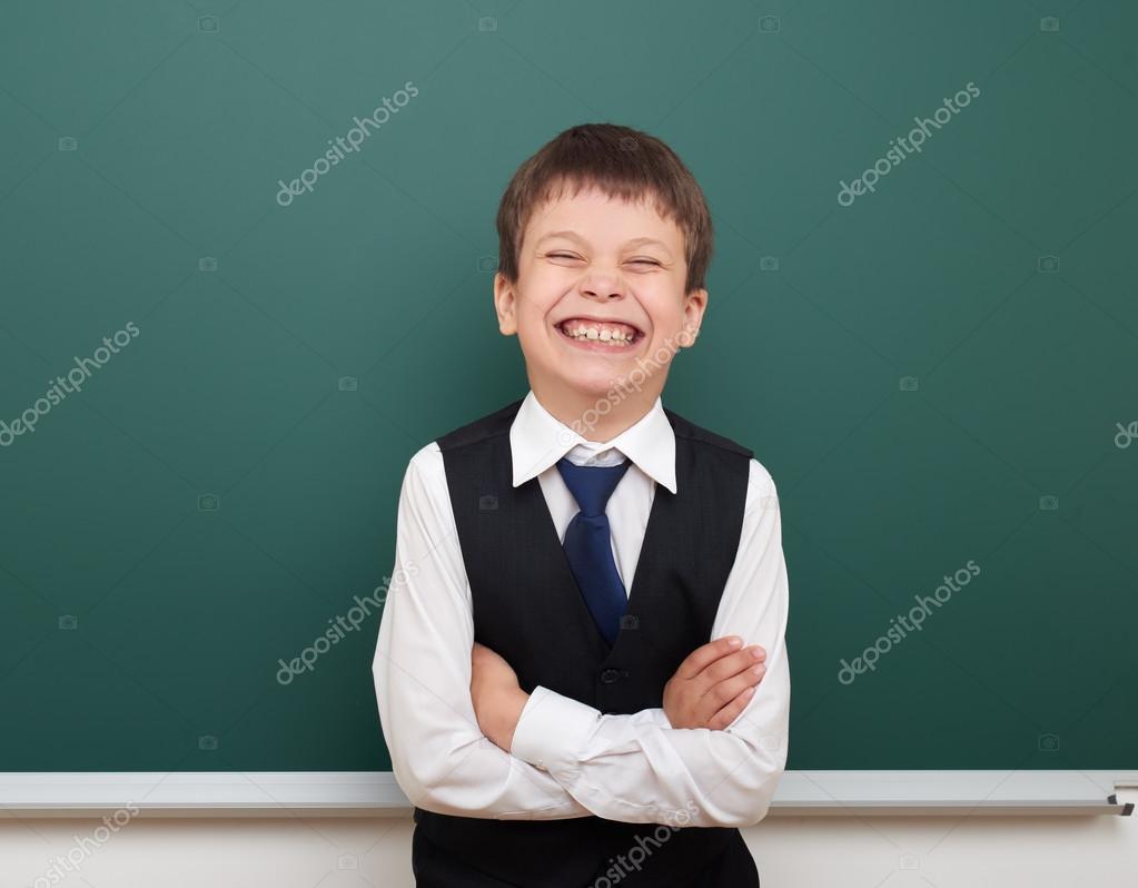 School student boy posing at the clean blackboard, grimacing and ...
