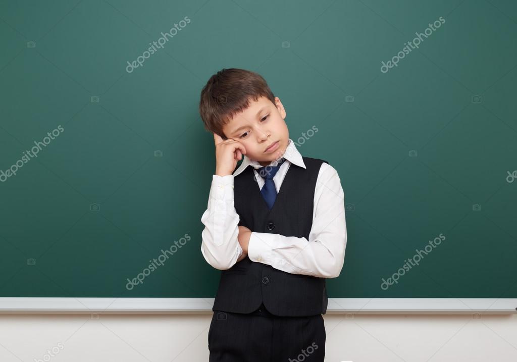 School student boy posing and think at the clean blackboard, grimacing ...