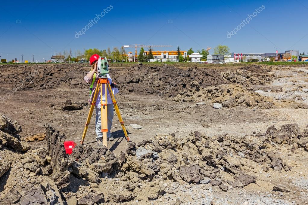 Female geodesist is working with total station on a building sit ...