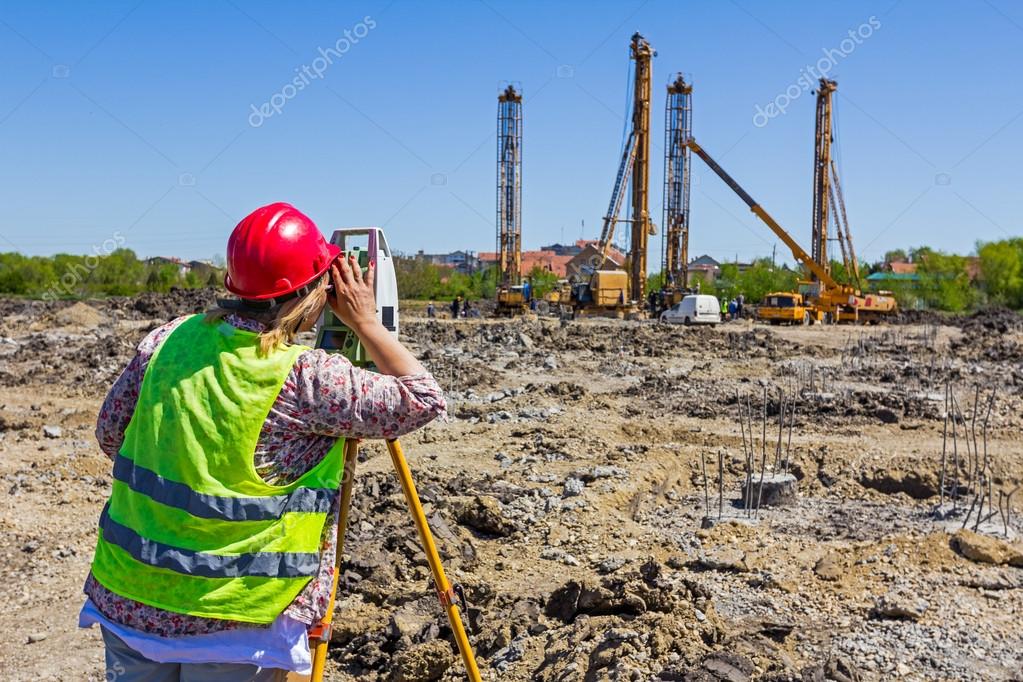 Female geodesist is working with total station on a building sit ...