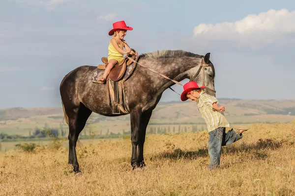 Two young happy kids riding a horse on farm, outdoor portrait on ...