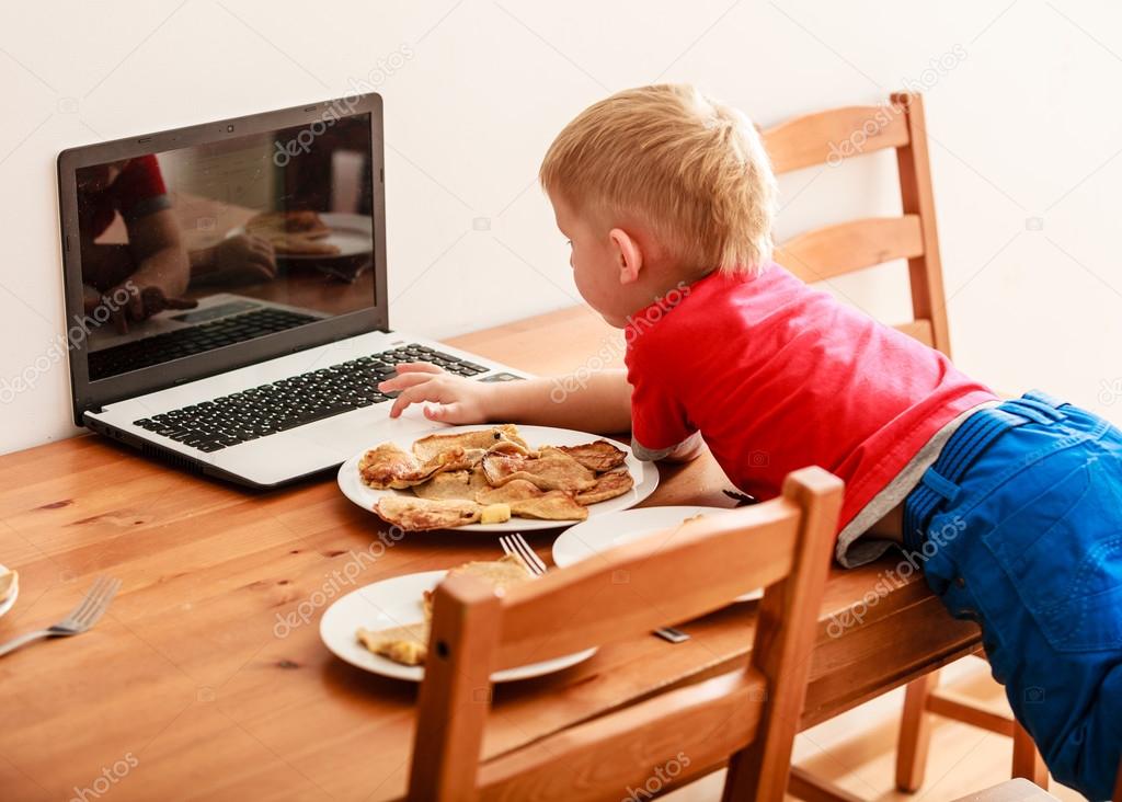 Little boy eating meal while using laptop Stock Photo by ©Voyagerix ...