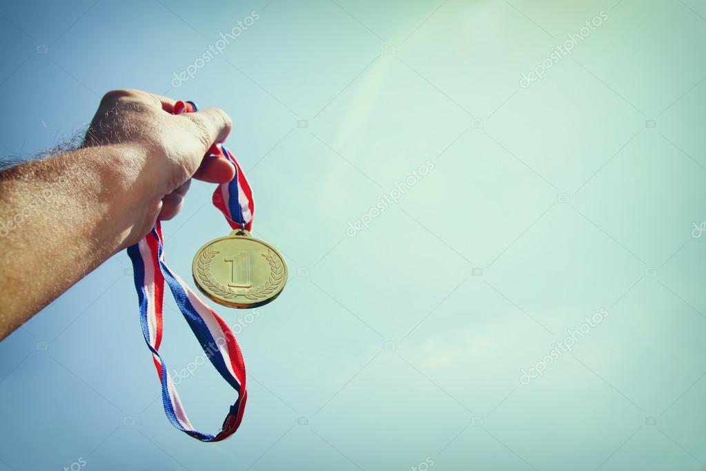 Man hand raised, holding gold medal against Sky. award and victory ...