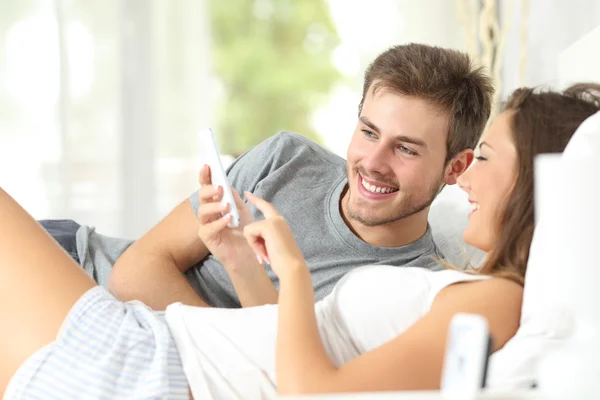 Couple sharing a smart phone on the bed - Stock Image - Everypixel