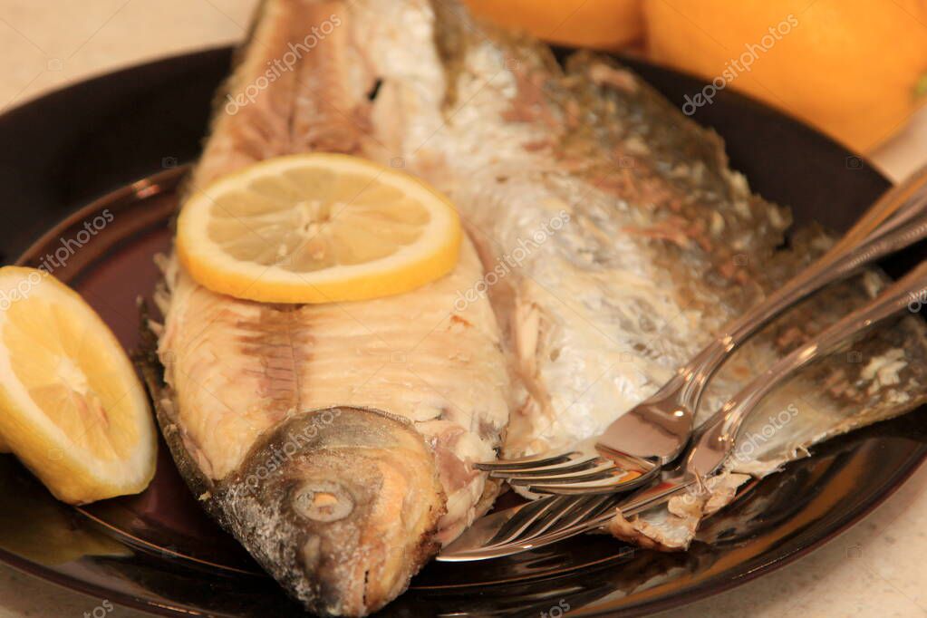 Pescado frito entero en un plato oscuro, decorado con limón. Pescado ...