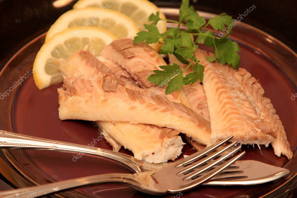 Filete de pescado cocido en un plato oscuro, decorado con limón ...