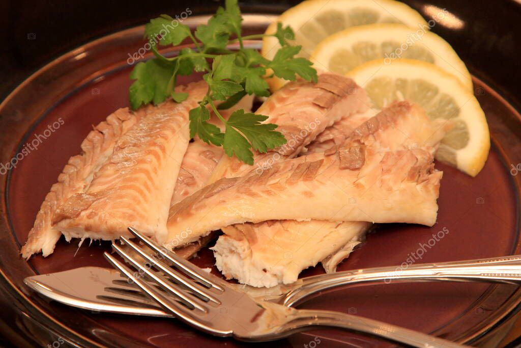 Filete de pescado cocido en un plato oscuro, decorado con limón ...