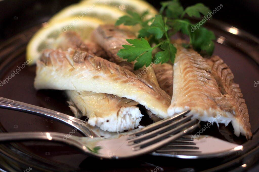 Filete de pescado cocido en un plato oscuro, decorado con limón ...