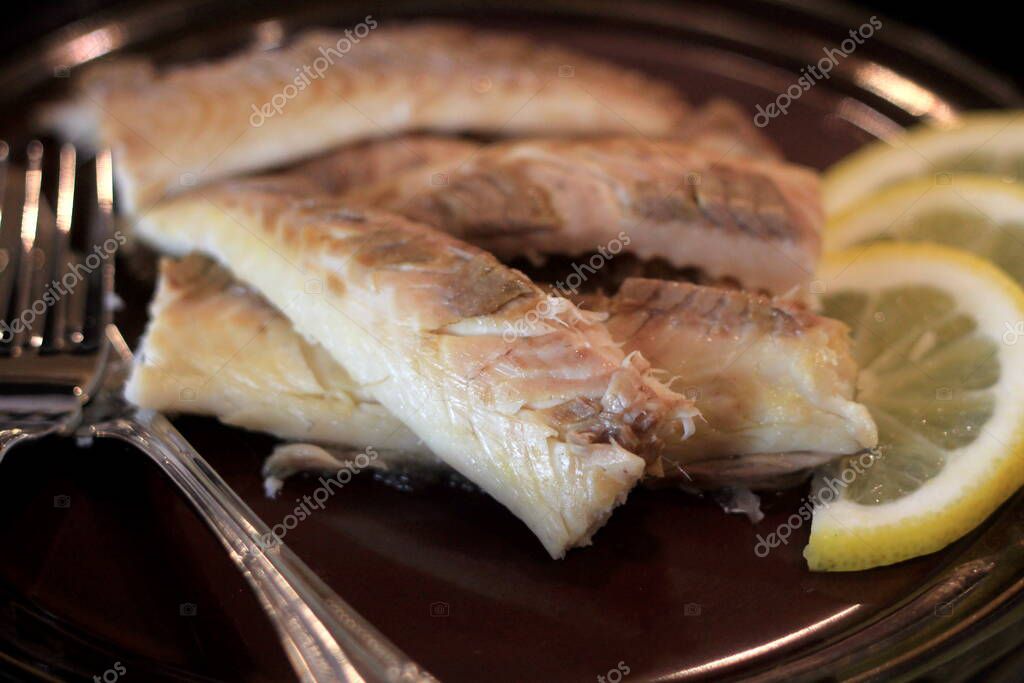 Filete de pescado cocido en un plato oscuro, decorado con limón ...