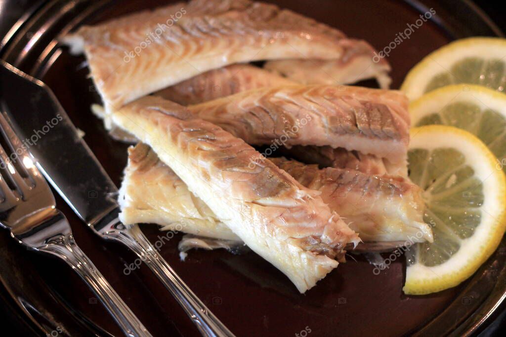 Filete de pescado cocido en un plato oscuro, decorado con limón ...